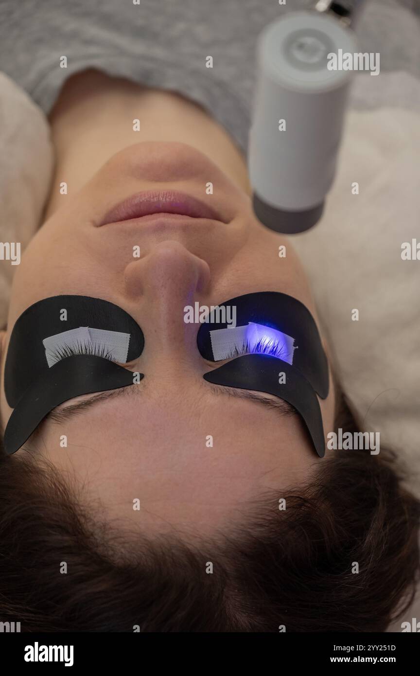 A woman undergoing eyelash extension procedure using an ultraviolet ...