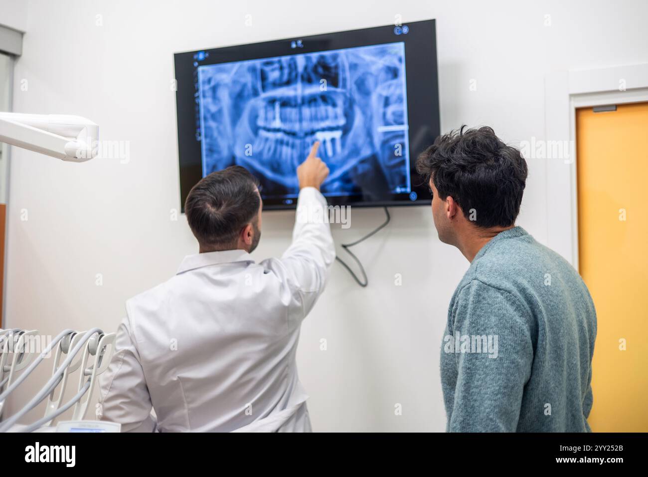 Dentist pointing at a teeth radiography on a monitor, explaining the ...