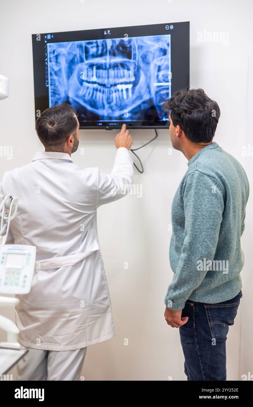 Dentist pointing at a large monitor featuring a detailed panoramic ...