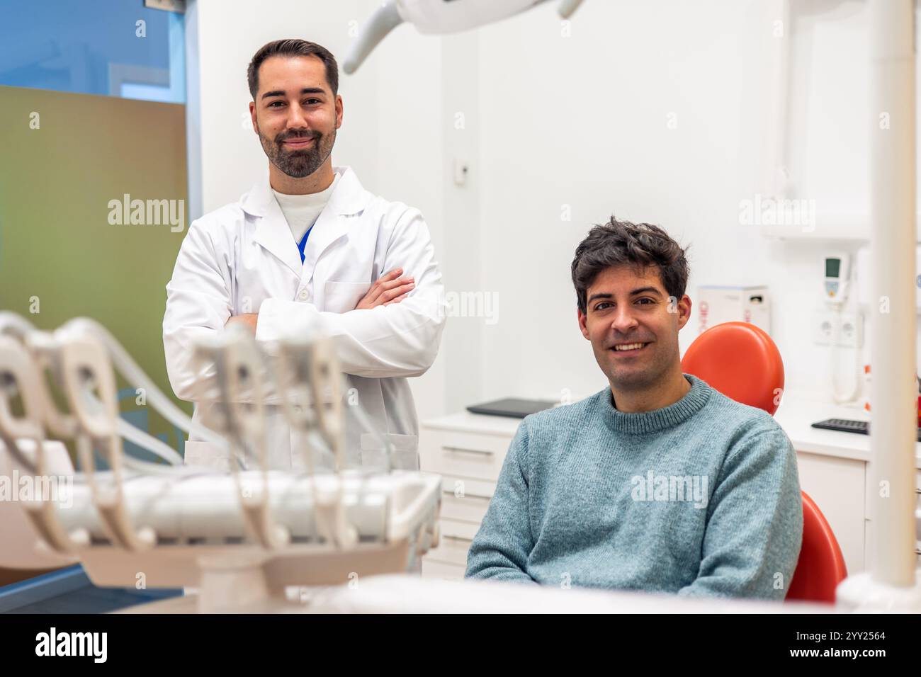 Portrait of a smiling dentist with arms crossed standing next to his ...