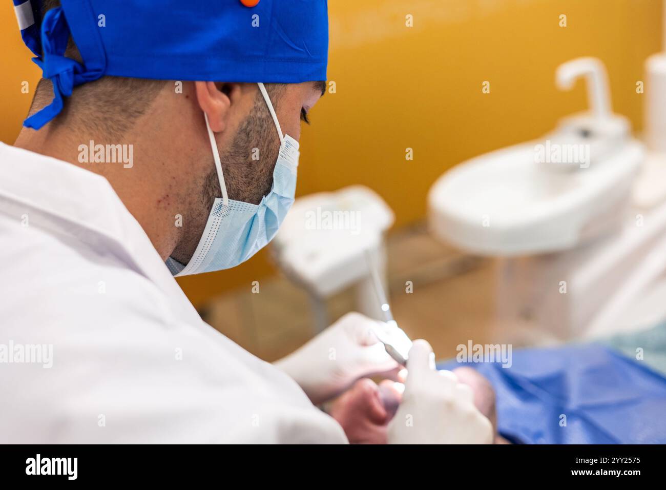 Dentist wearing a surgical cap, mask, and gloves is carefully ...