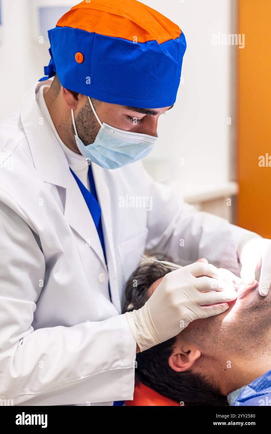 Dentist wearing a surgical mask, cap, and gloves is carefully examining ...