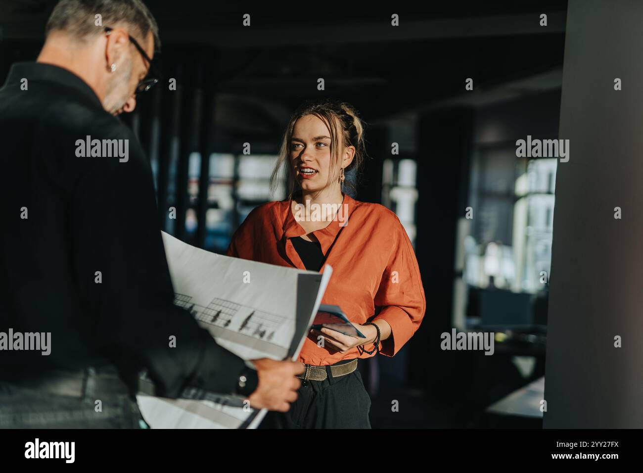 Two business people engage in a discussion over architectural plans in ...