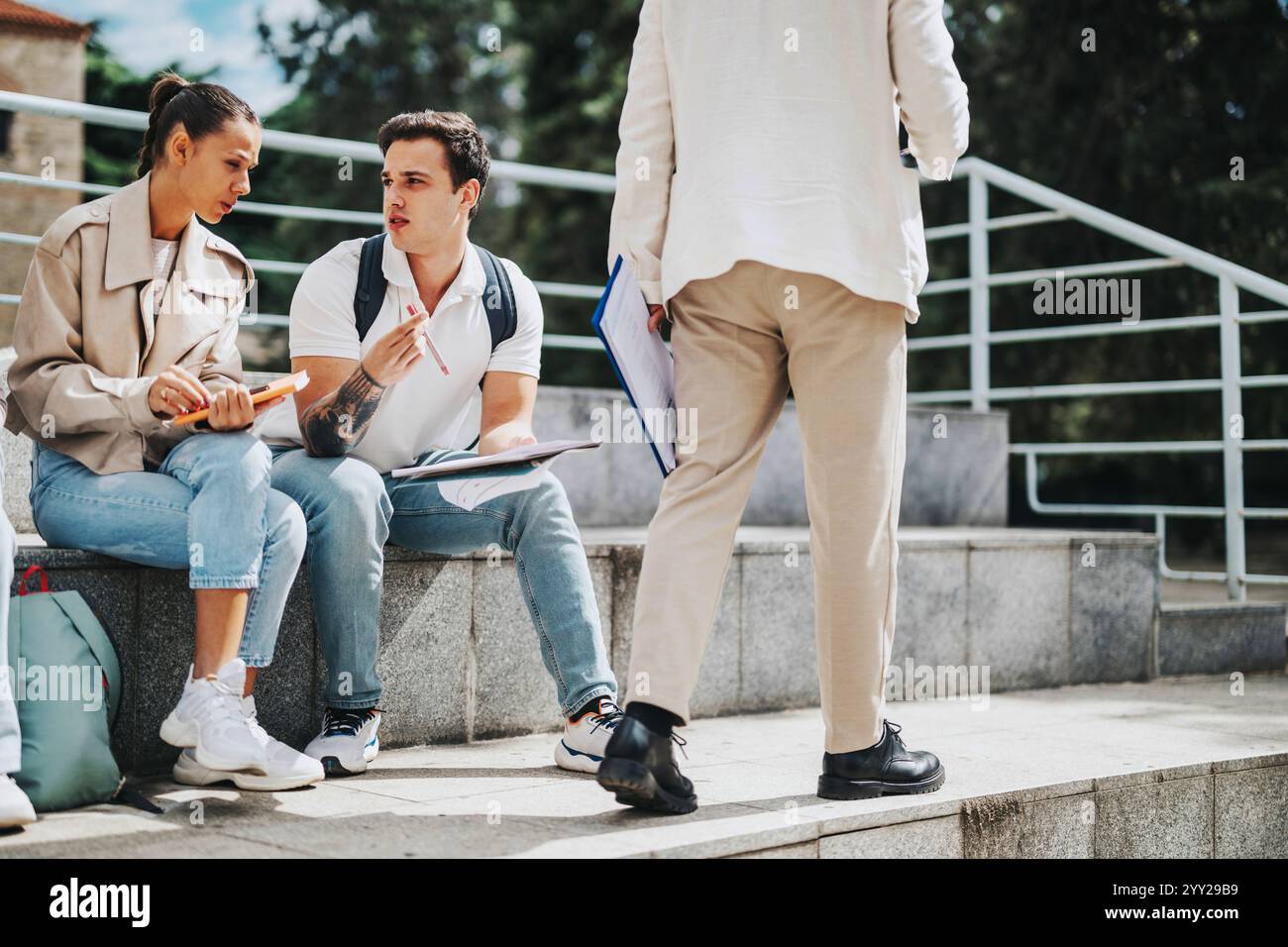 High school students collaborating with professor outdoors on campus ...