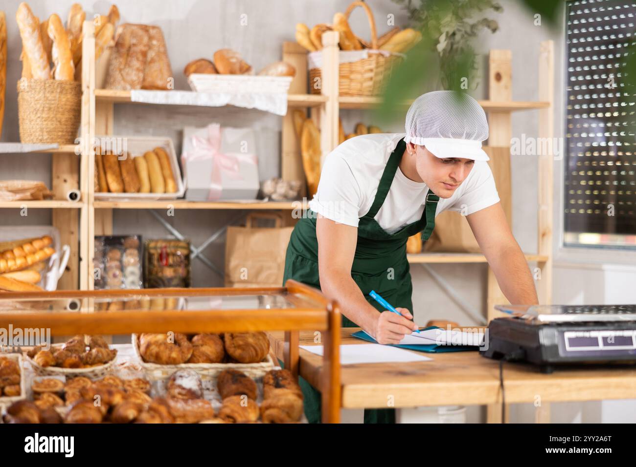 Young baker reading documents and writing notes on paper in the ...