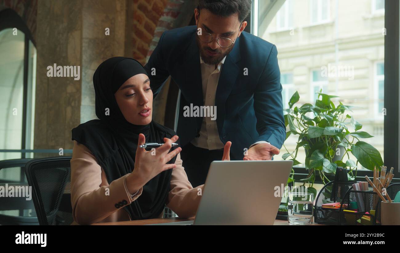 Male businessman teach female muslim worker hijab in office mentor leader help laptop work ...