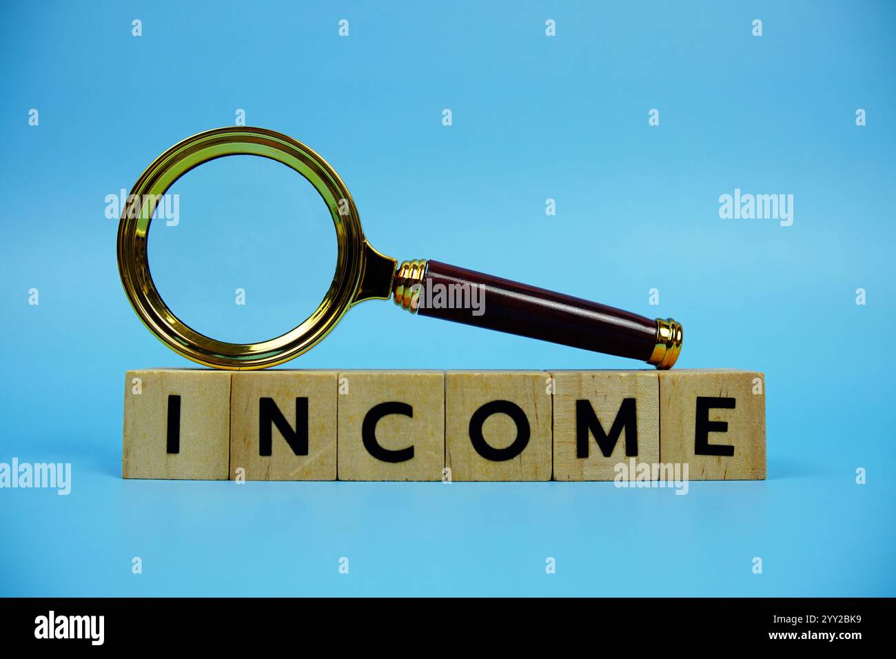 Income with wooden blocks alphabet letters and Magnifying glass on blue ...