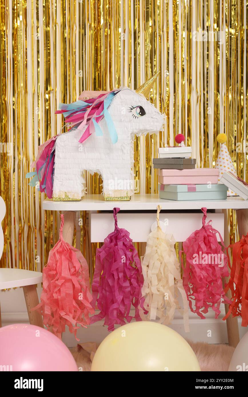 Bright pinata in shape of unicorn and party accessories against foil ...