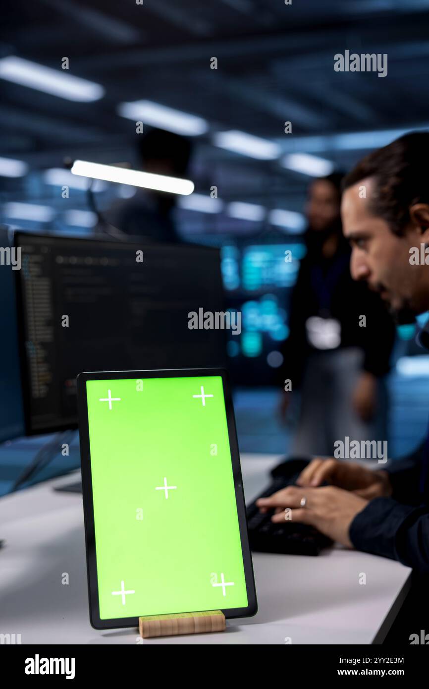 Focus on green screen tablet used by admin in blurry background to do maintenance in server farm ...