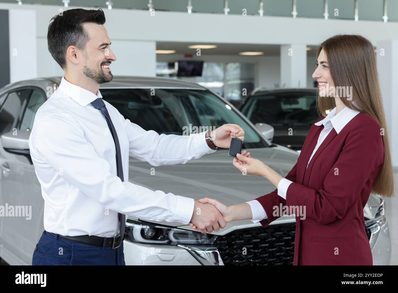 Salesman giving key to client near new car in salon Stock Photo - Alamy