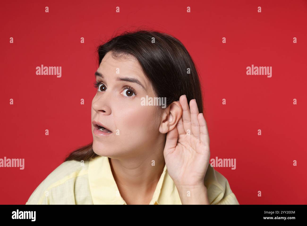 Woman showing hand to ear gesture on red background Stock Photo - Alamy