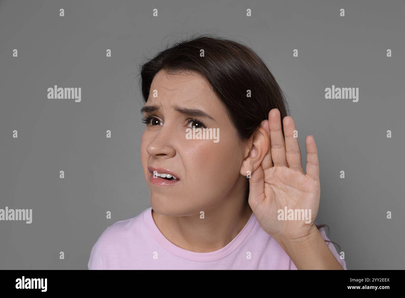 Woman showing hand to ear gesture on grey background Stock Photo - Alamy