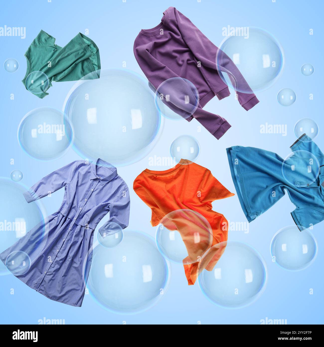 Different clothes flying among soap bubbles on light blue background ...