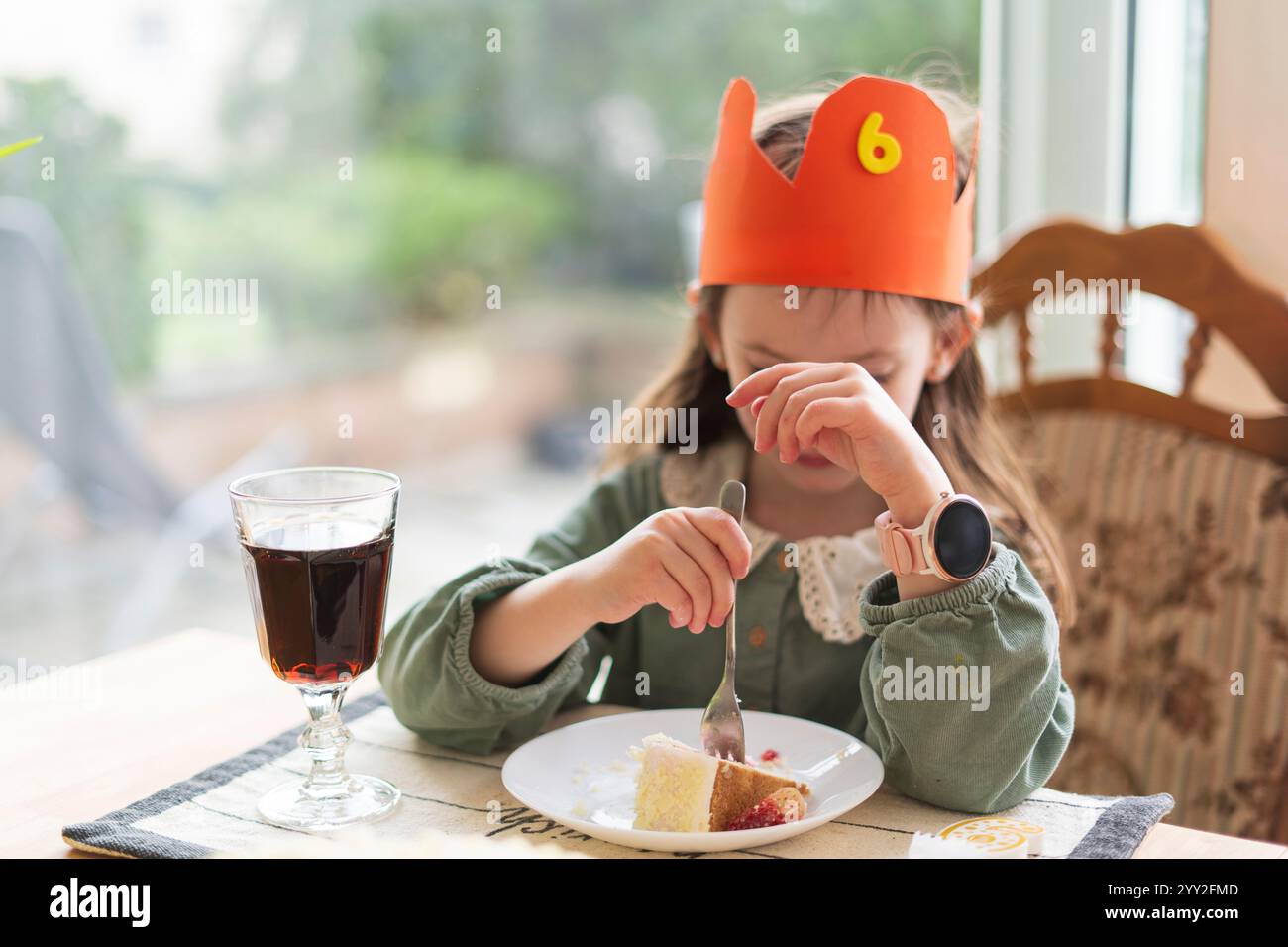 A cute little smiling girl in a fancy dress and crown sits at a festive ...