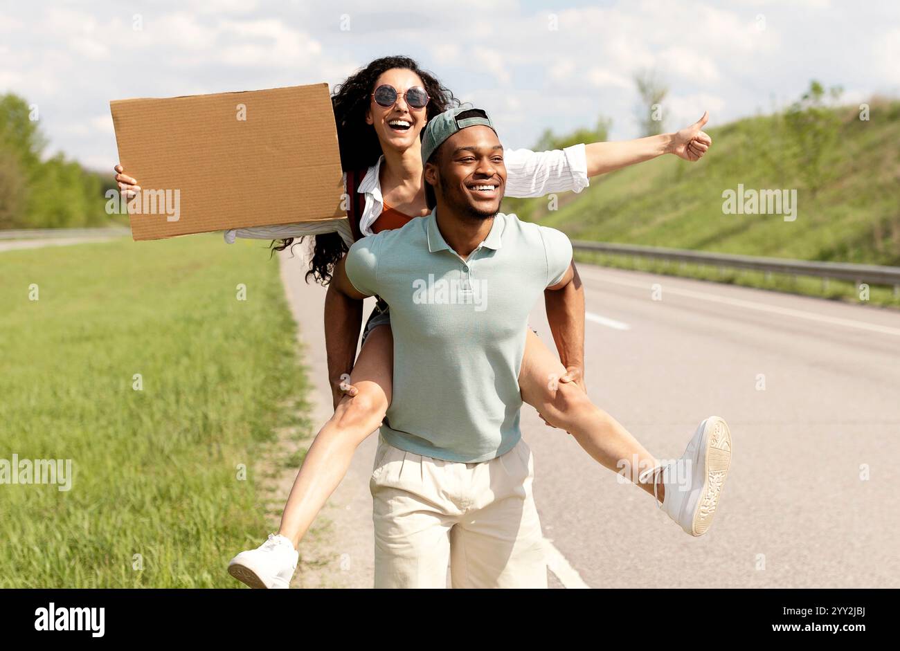 Black guy giving piggyback ride to his girlfriend, hitchhiking on road ...