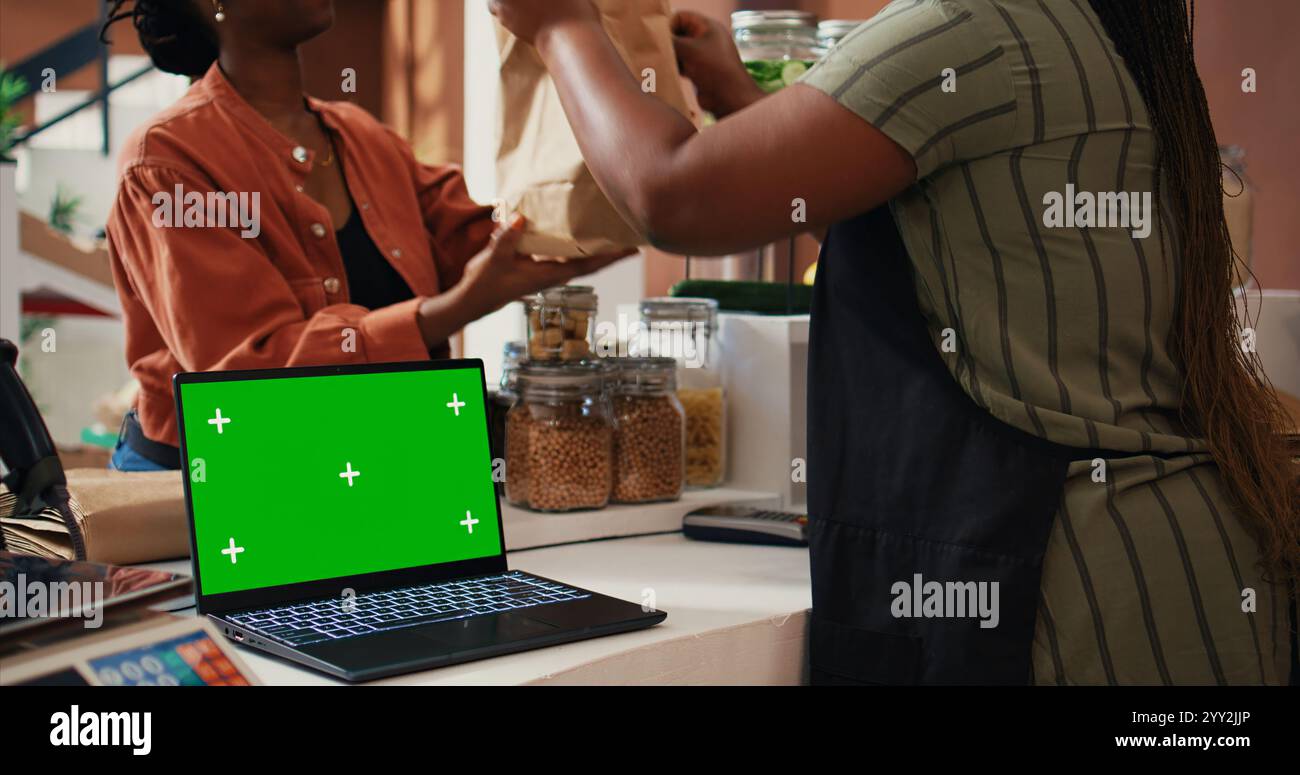 Merchant selling eco goods next to greenscreen laptop at grocery store ...