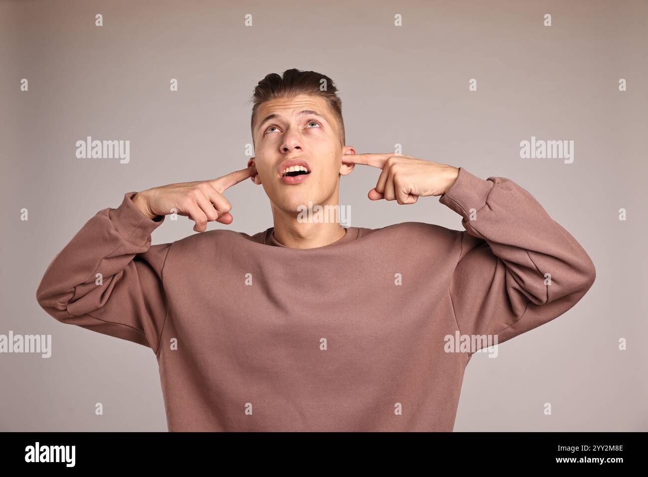 Annoyed young man covering his ears due to loud sound on light grey background Stock Photo - Alamy