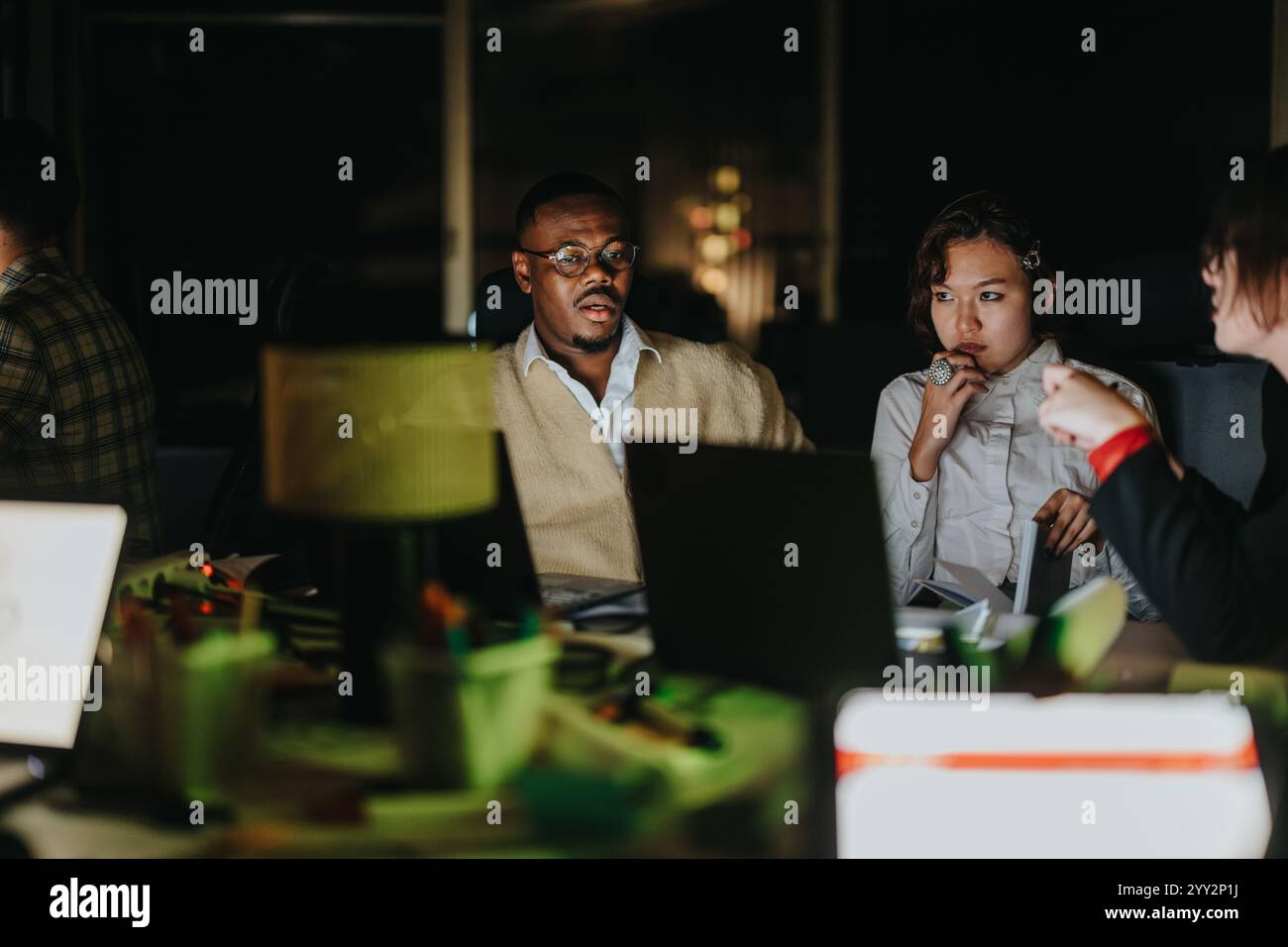 Multiracial colleagues work late at night in an office, discussing ...