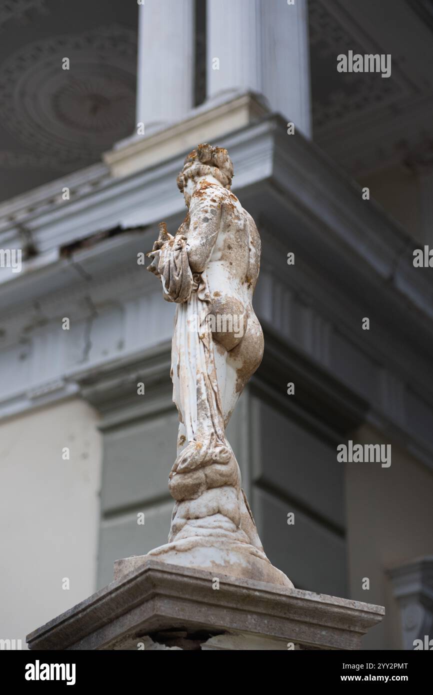 An antique statue made of white stone with a layer of old dirt stands ...