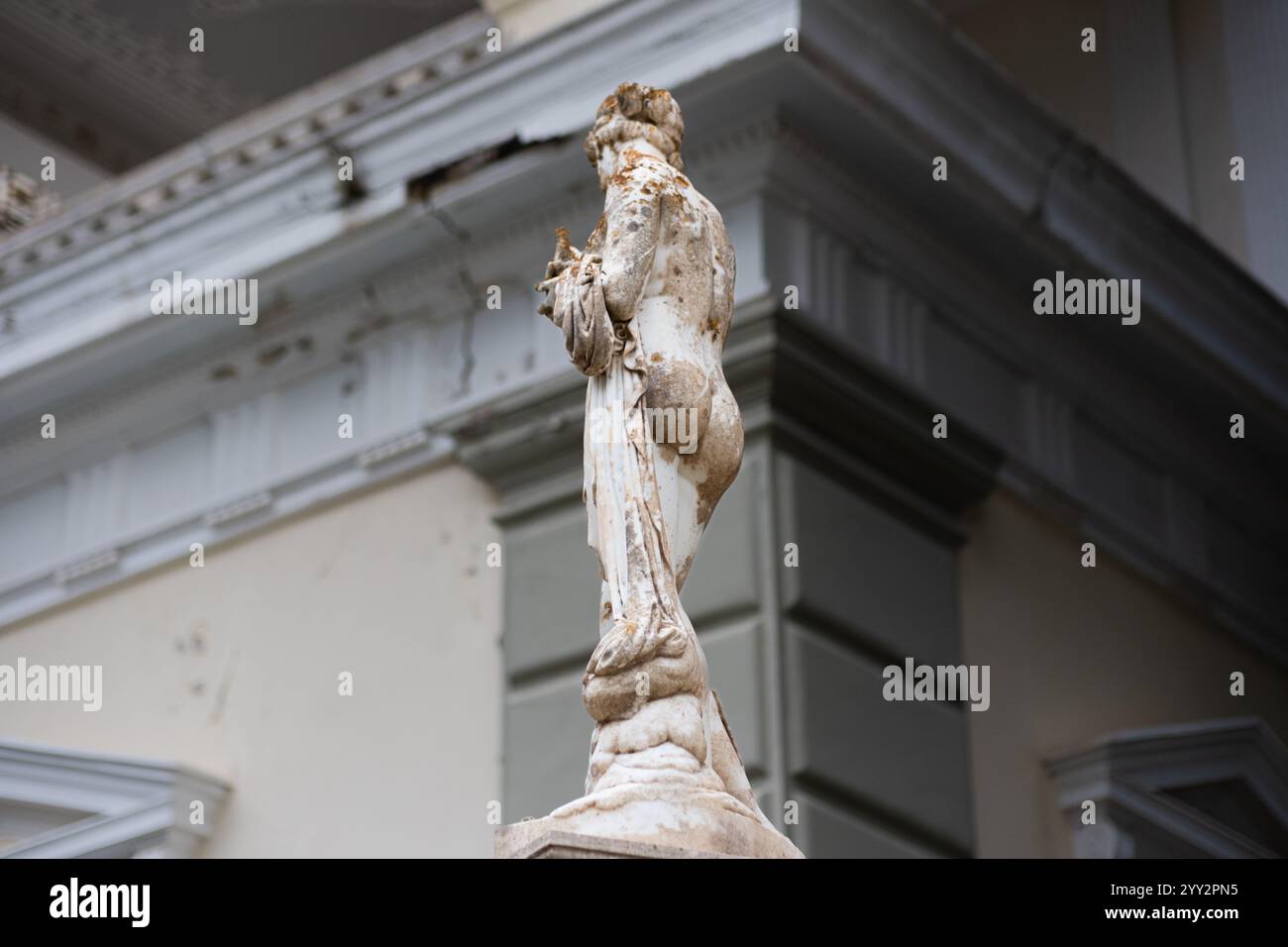 An antique statue made of white stone with a layer of old dirt stands ...