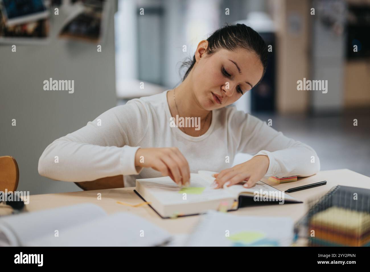 Focused student studying with notes at a desk in library environment ...