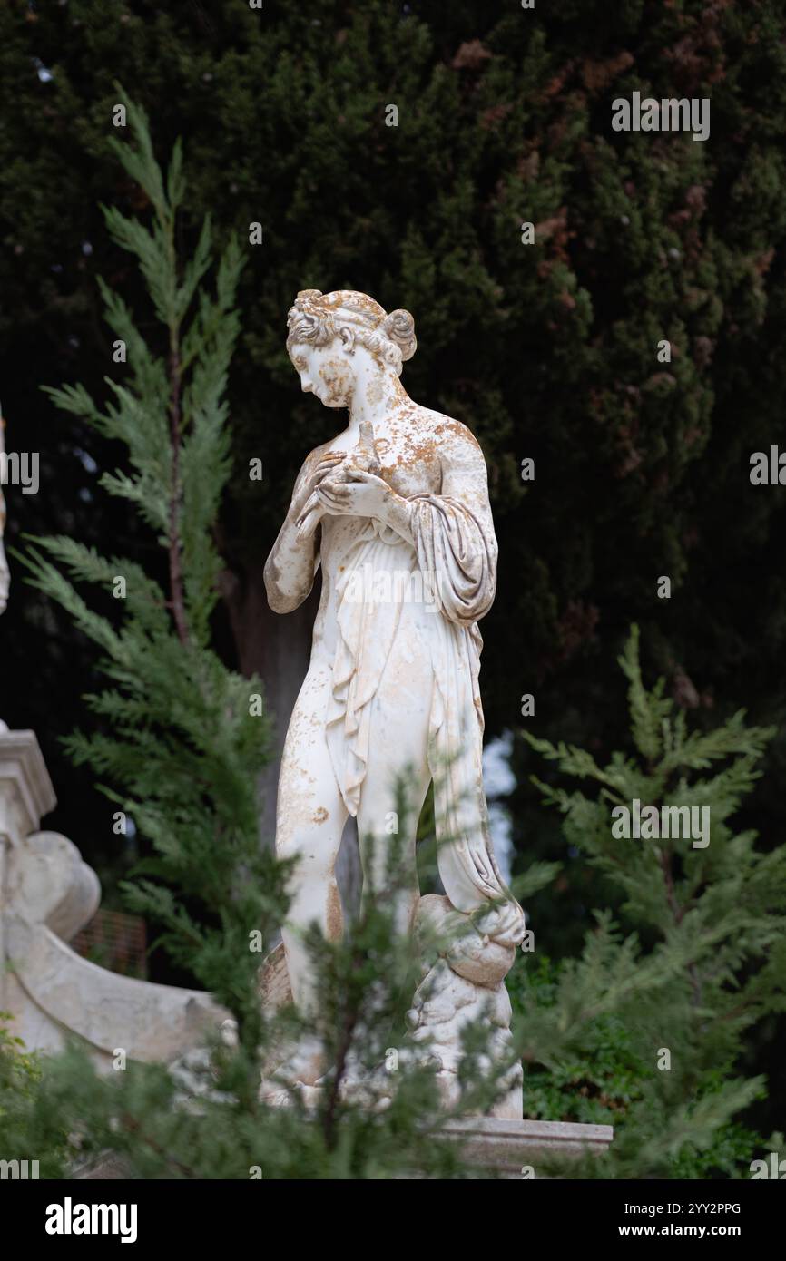 An antique statue made of white stone with a layer of old dirt stands ...