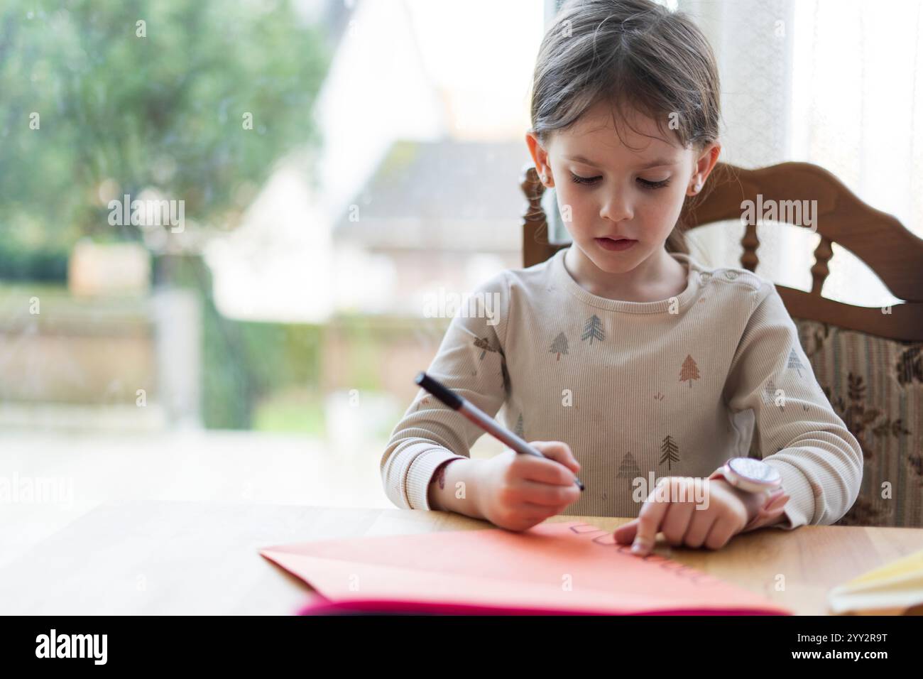 Little cute girl doing origami sitting at the table with a big window ...
