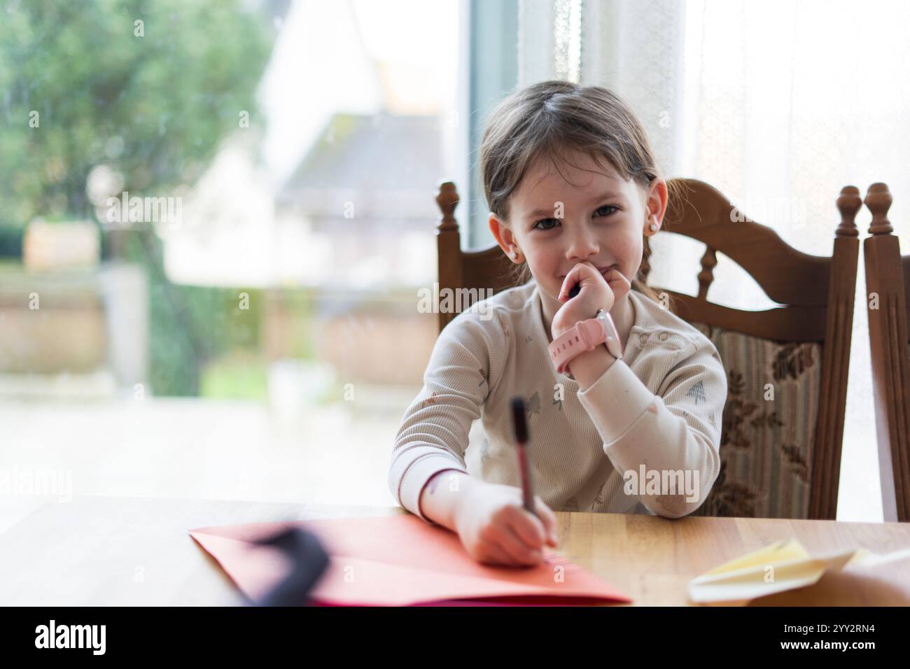 Little cute girl doing origami sitting at the table with a big window ...