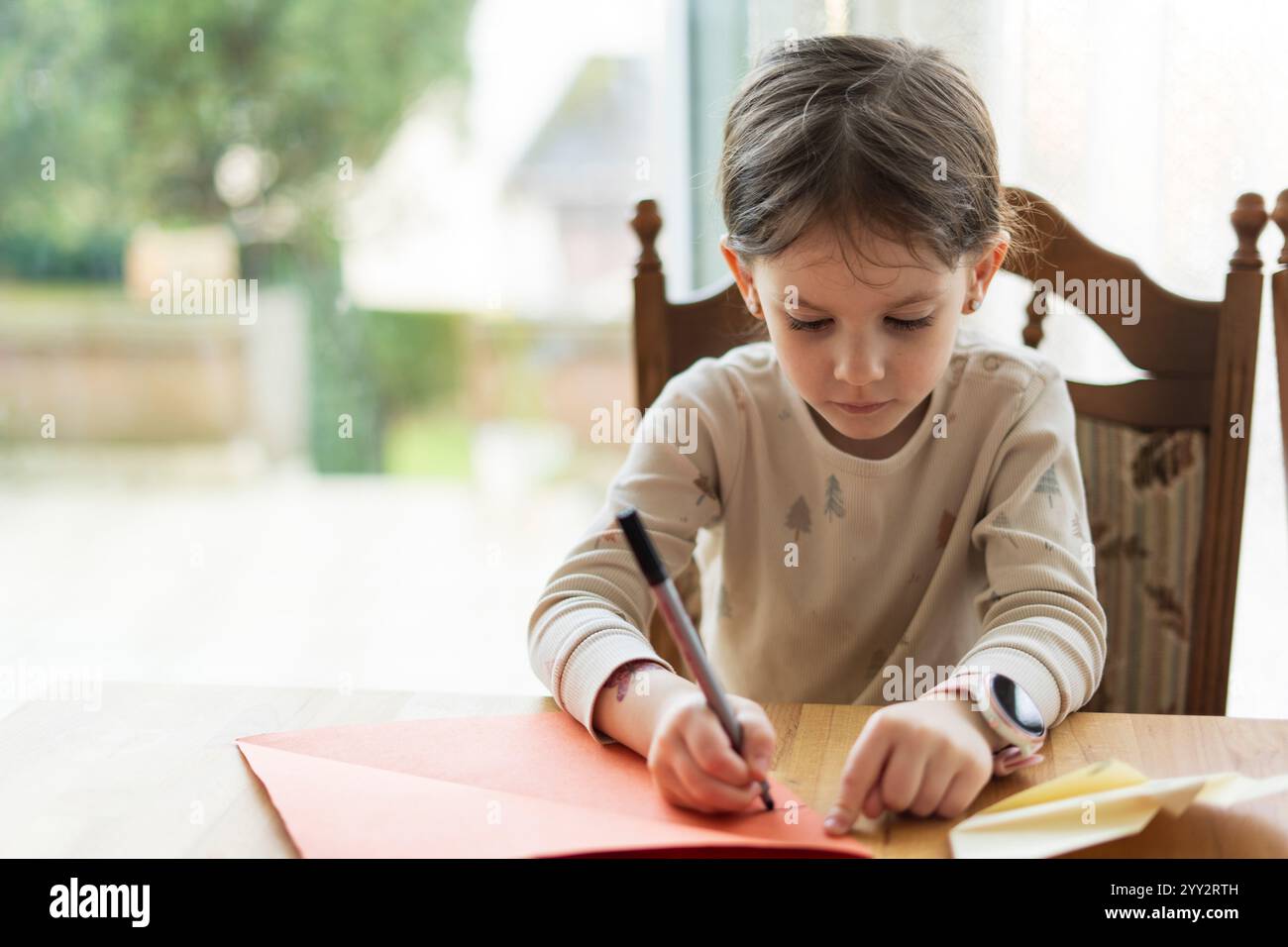 Little cute girl doing origami sitting at the table with a big window ...