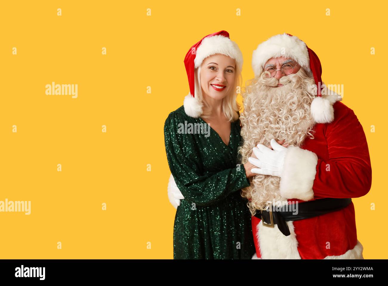 Santa Claus and beautiful mature woman in Christmas hats on yellow ...