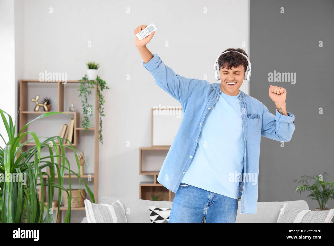 Happy young man in headphones with air conditioner remote control ...