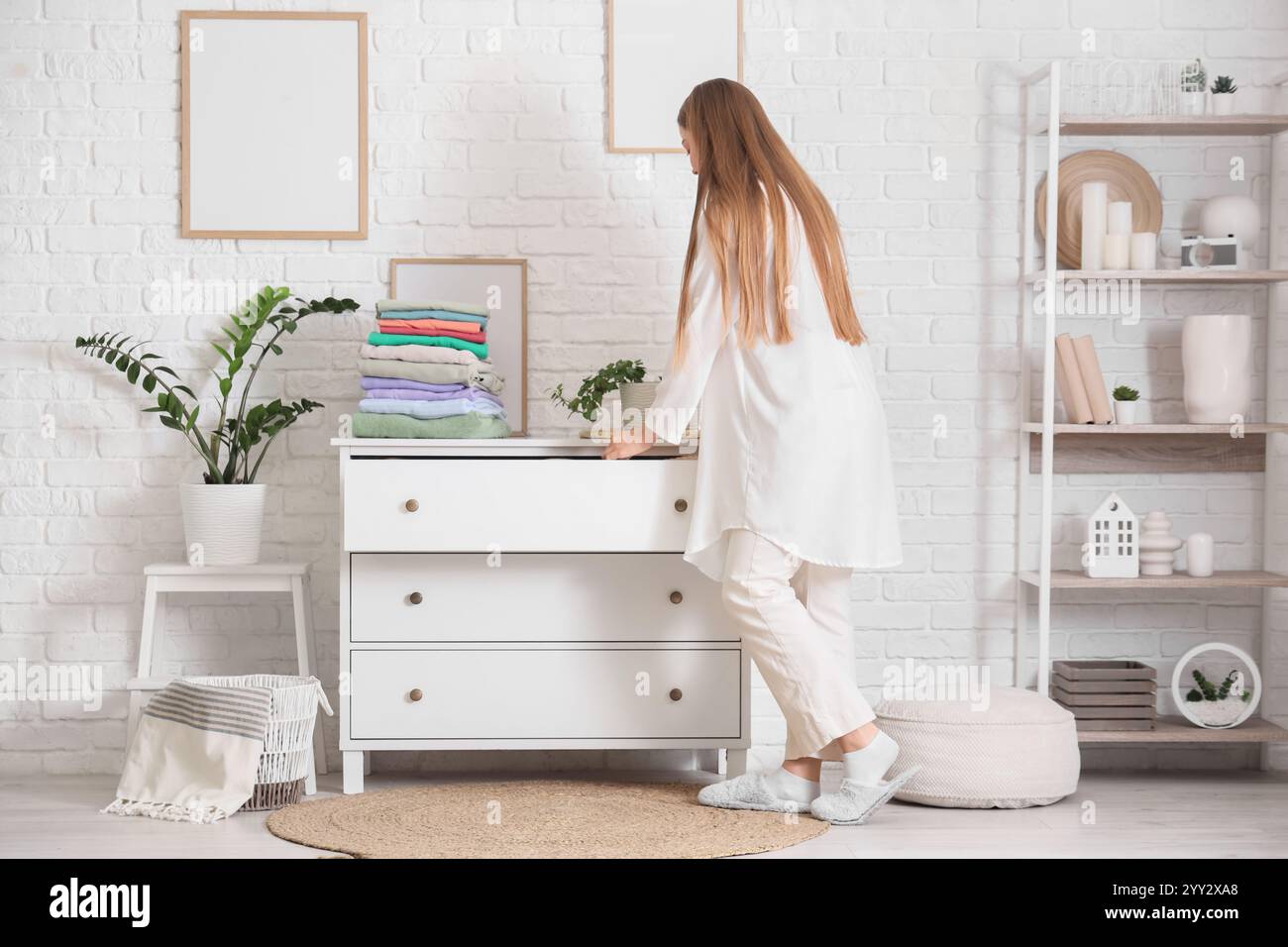Young woman putting stack of clothes into drawer at home, back view ...