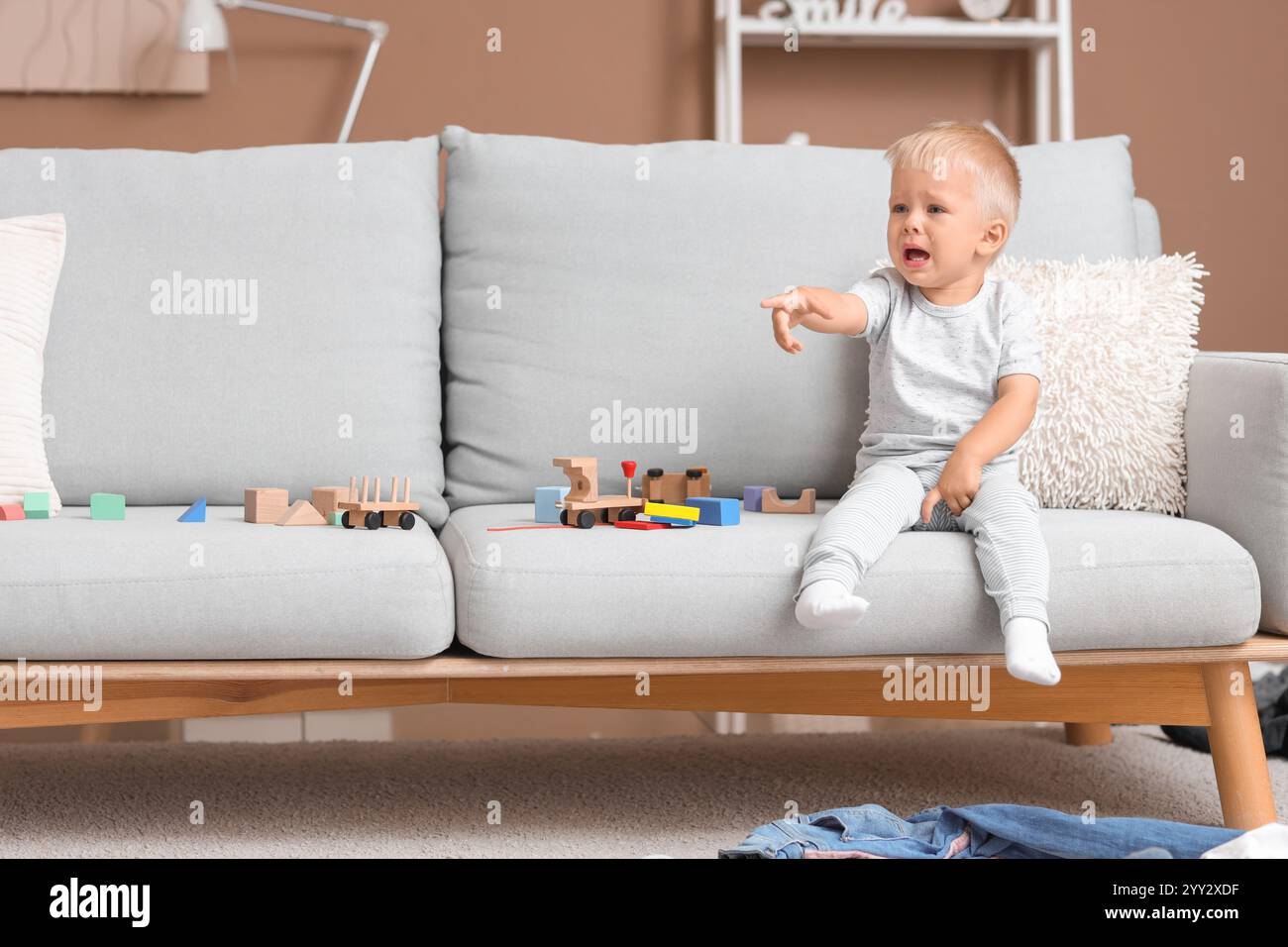 Baby boy crying on sofa in messy room Stock Photo - Alamy