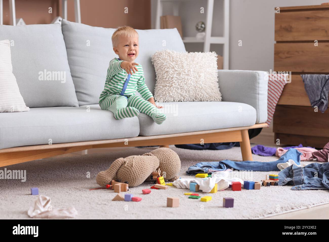 Crying baby boy on sofa in messy room Stock Photo - Alamy