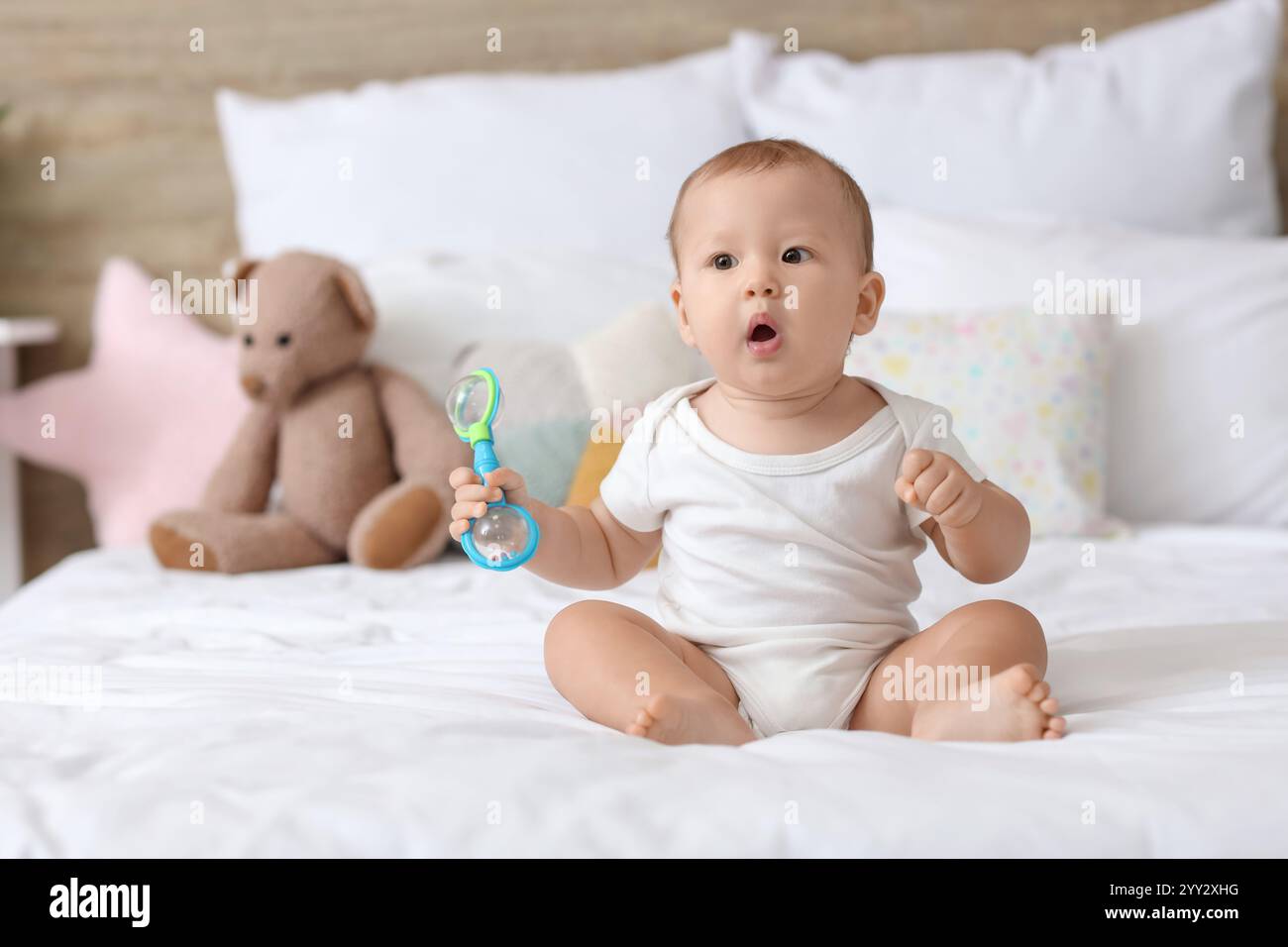 Cute baby with rattle sitting on bed at home Stock Photo - Alamy