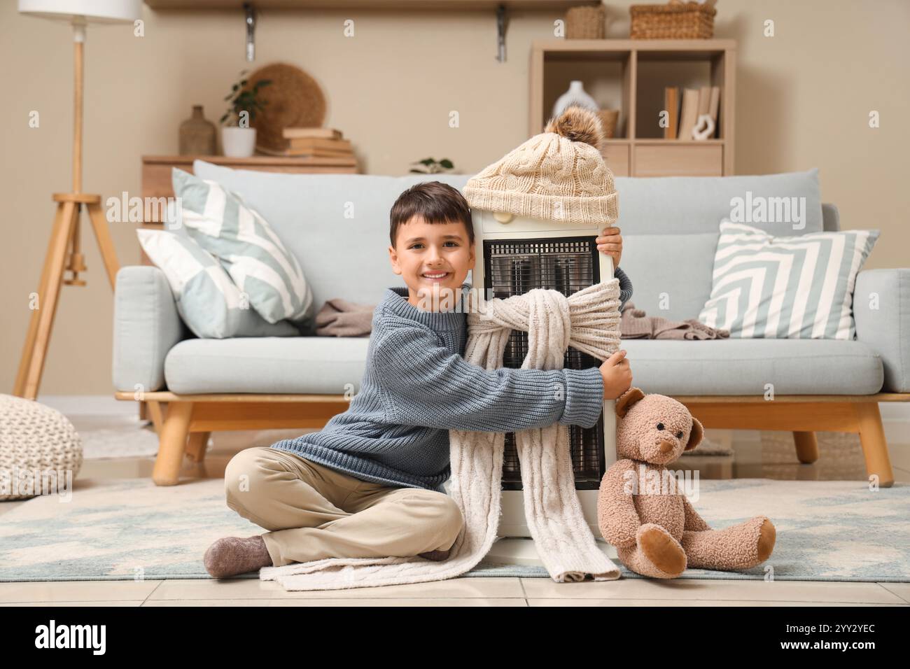 Cute boy hugging electric heater with warm hat and scarf at home Stock ...
