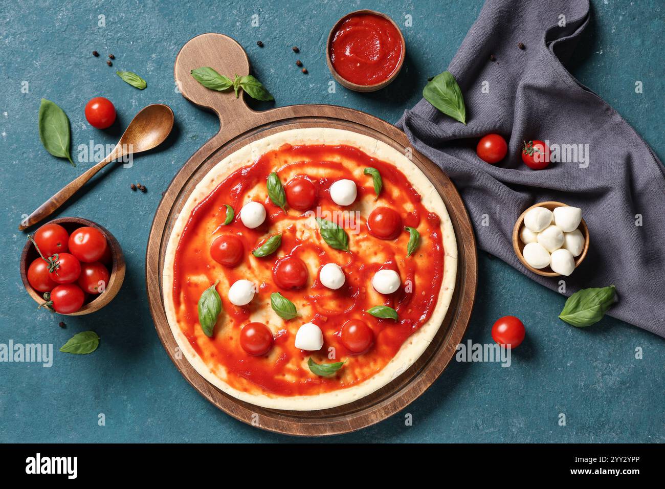 Wooden board with raw pizza with ingredients on turquoise grunge ...