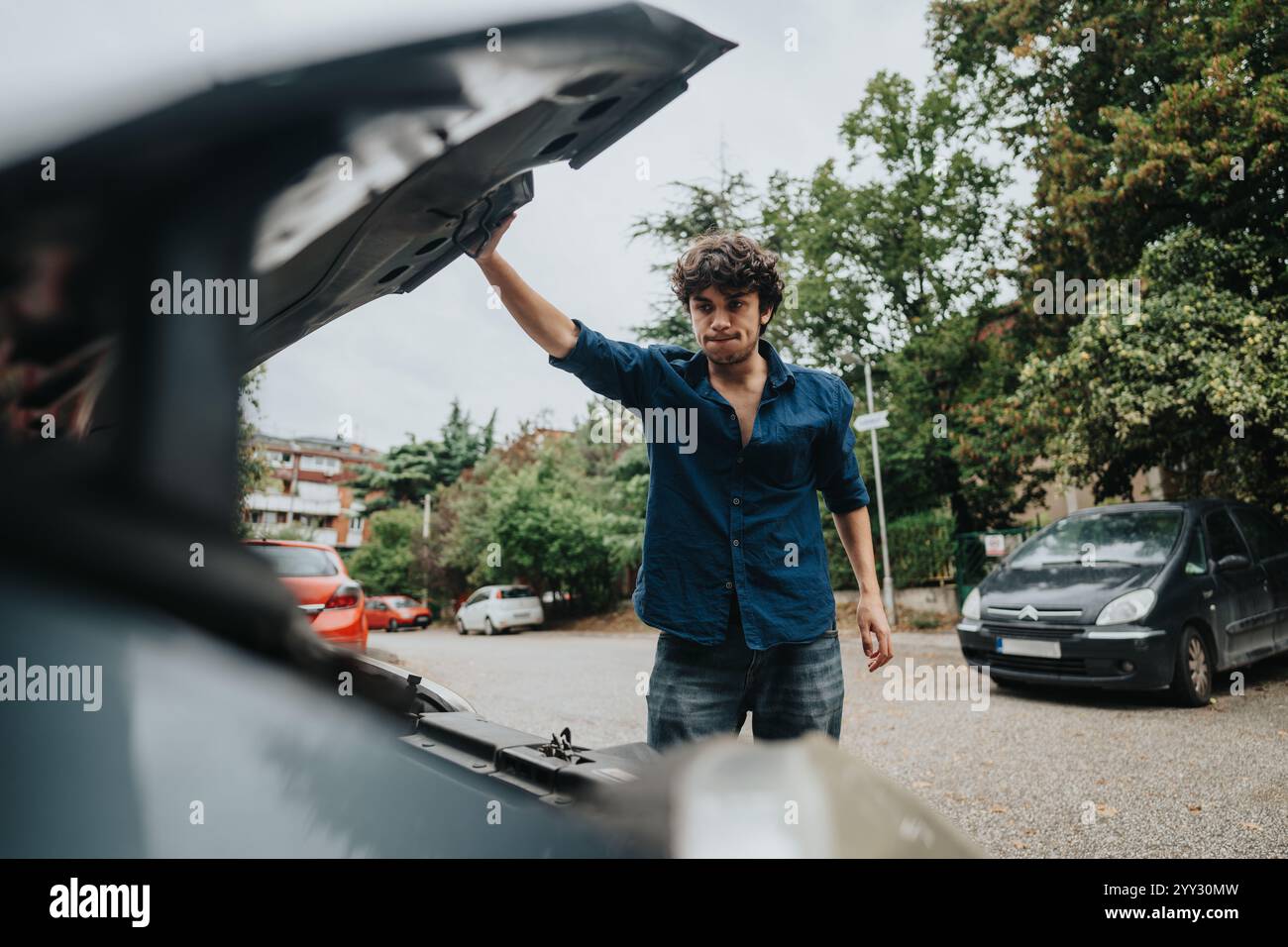 Frustrated man inspecting car engine in outdoor parking lot Stock Photo ...