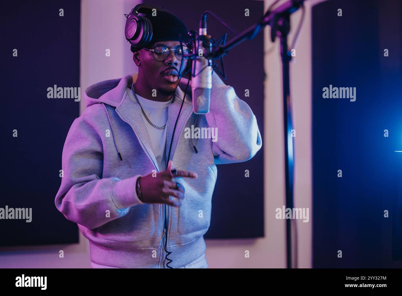 Musician in recording studio singing into microphone with headphones on ...