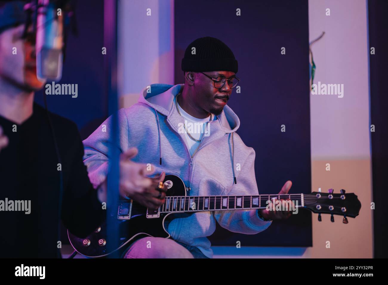 A young musician wearing a hoodie and beanie plays an electric guitar ...