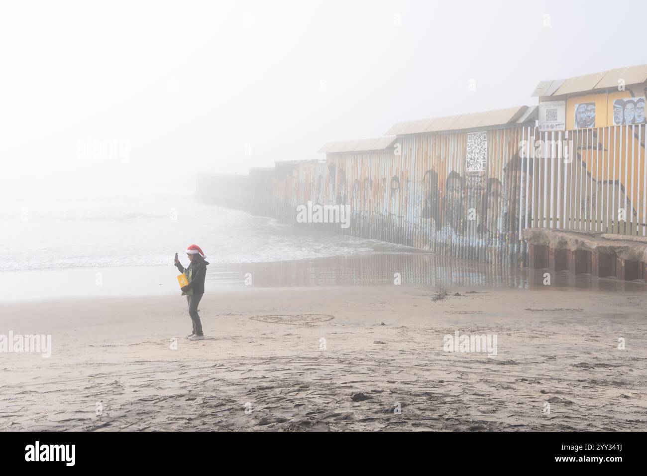Lia Bolanos wears a Santa hat as she takes a selfie next to the border ...