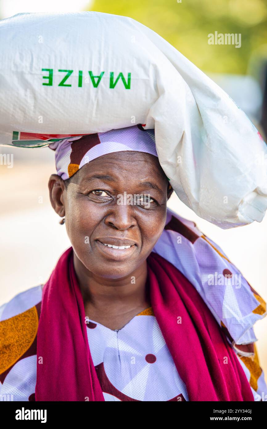 african woman carry a bag of maize on her head in the street, happy ...