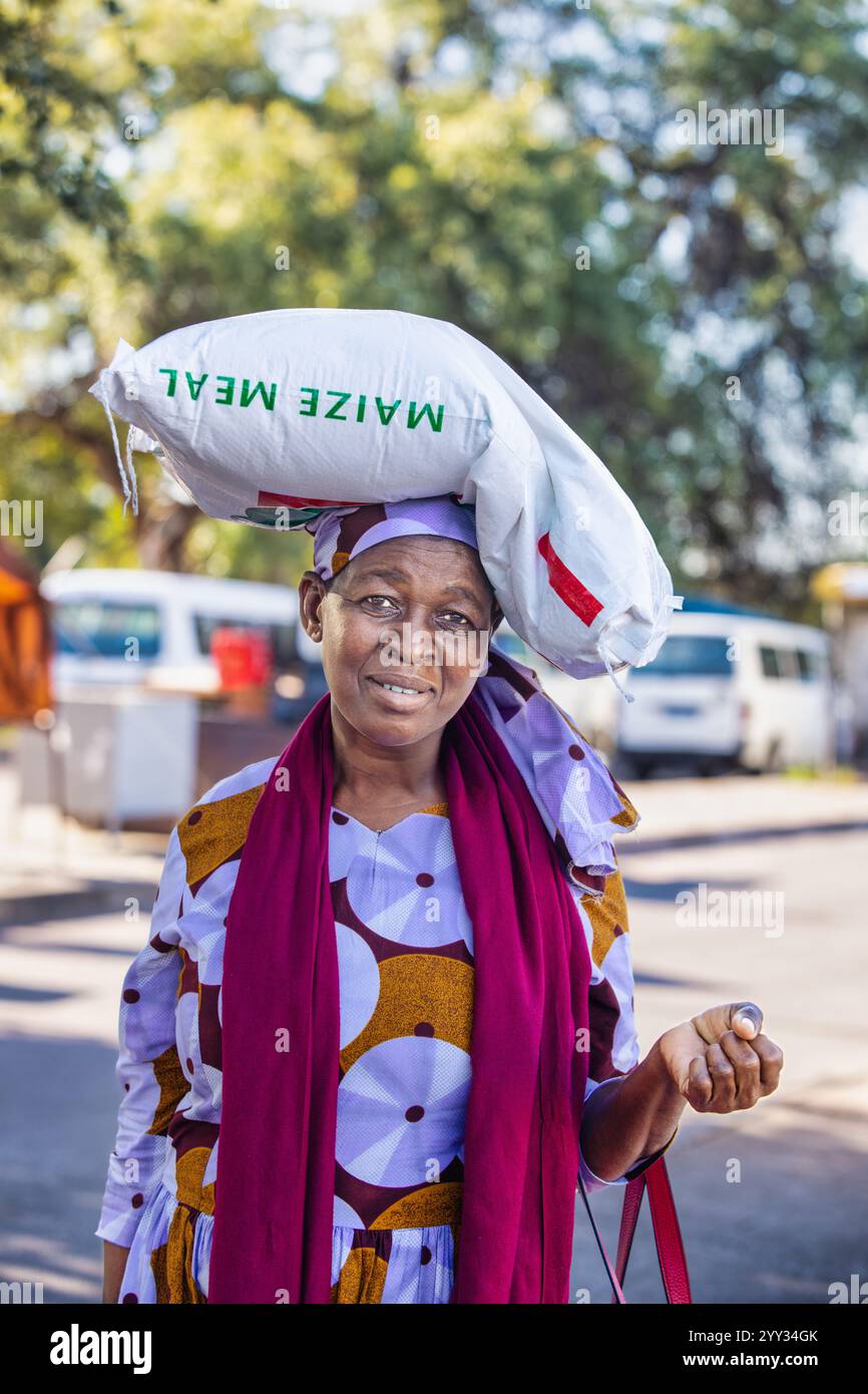 african woman carry a bag of maize on her head in the street, happy ...