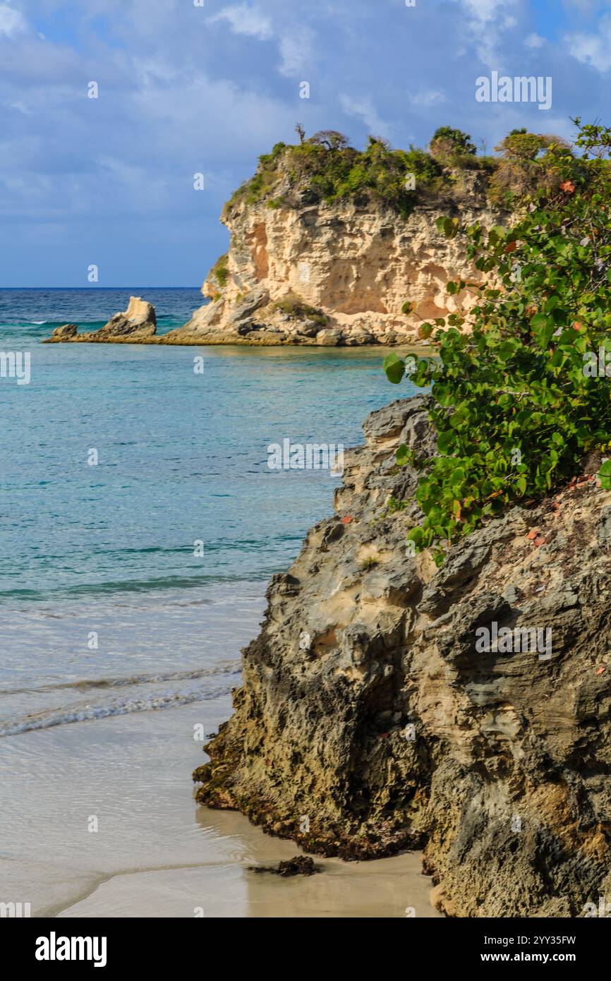 A rocky cliff overlooks the ocean. The water is calm and the sky is ...