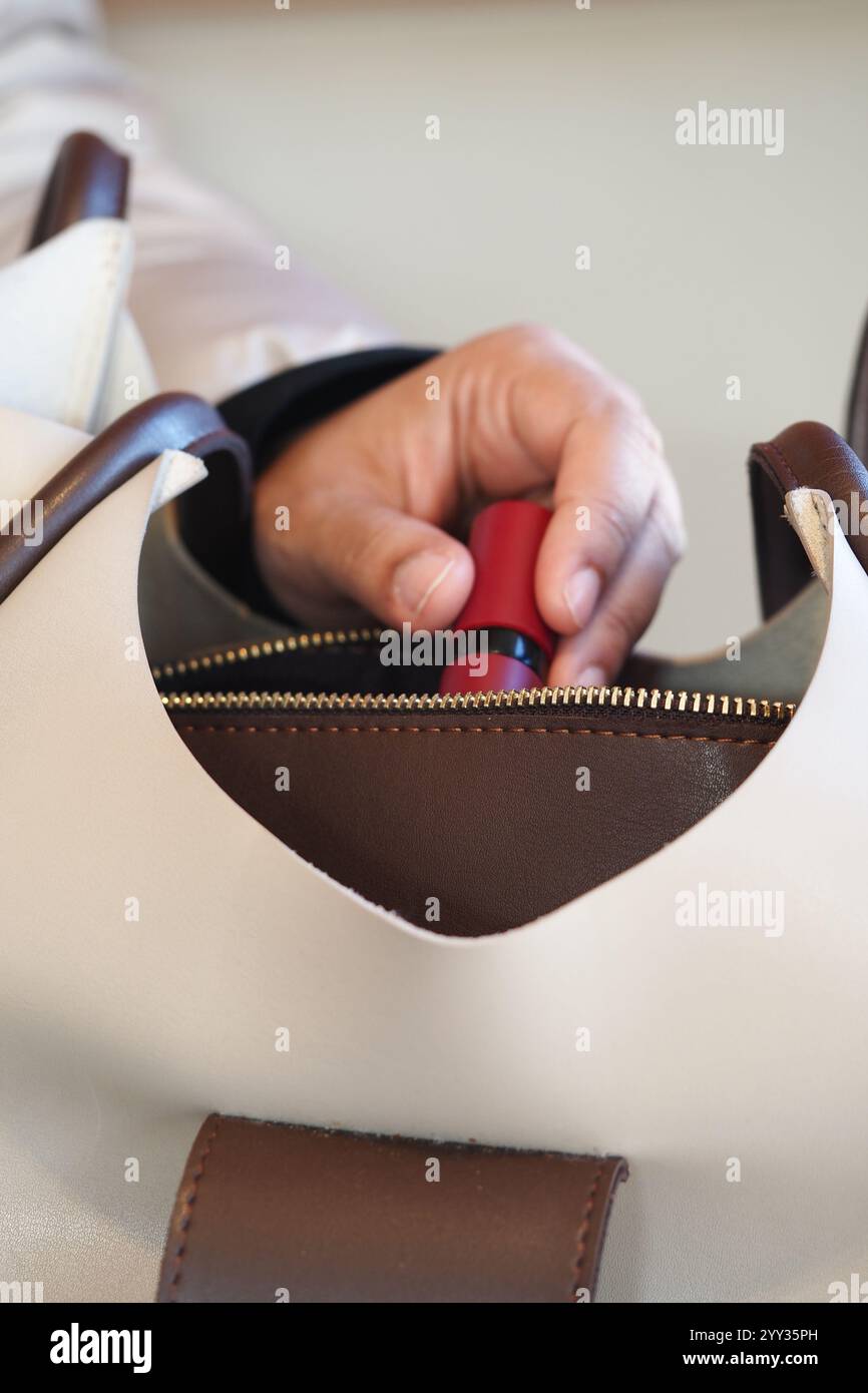 Woman hand is gracefully holding a lip gloss positioned above a purse ...