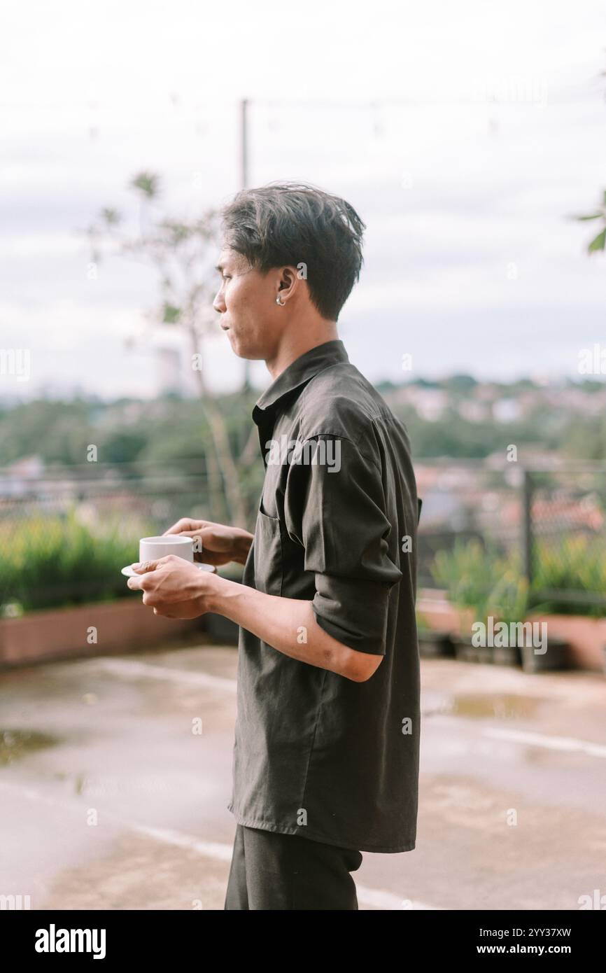 A Southeast Asian man enjoying a sip of coffee on a peaceful morning ...