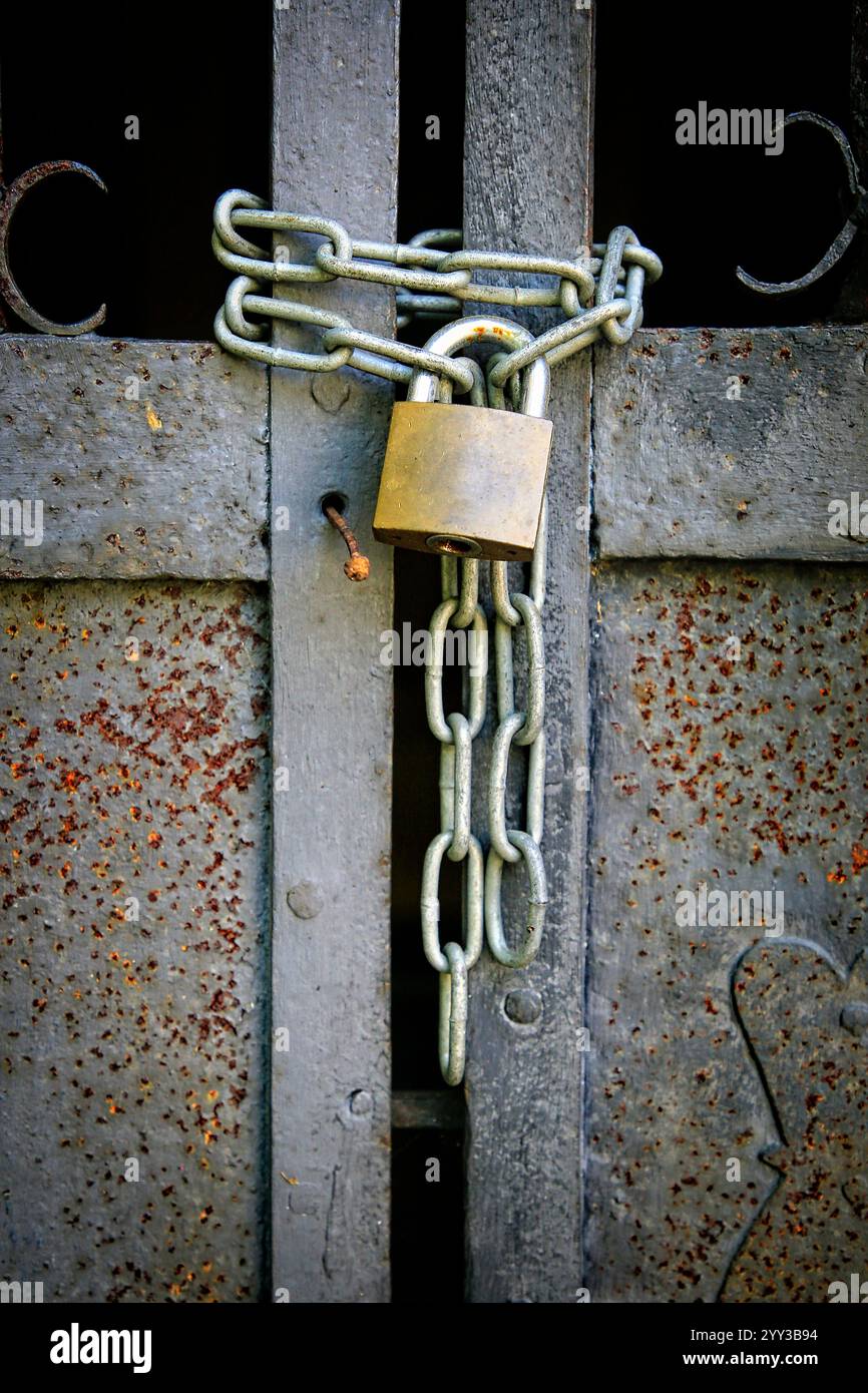 Old locked iron gate secured with a padlock and chain, seen close up ...