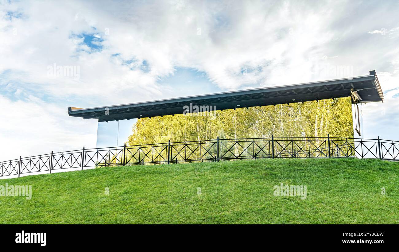 Modern mirrored building reflects trees on green hill topped with a ...