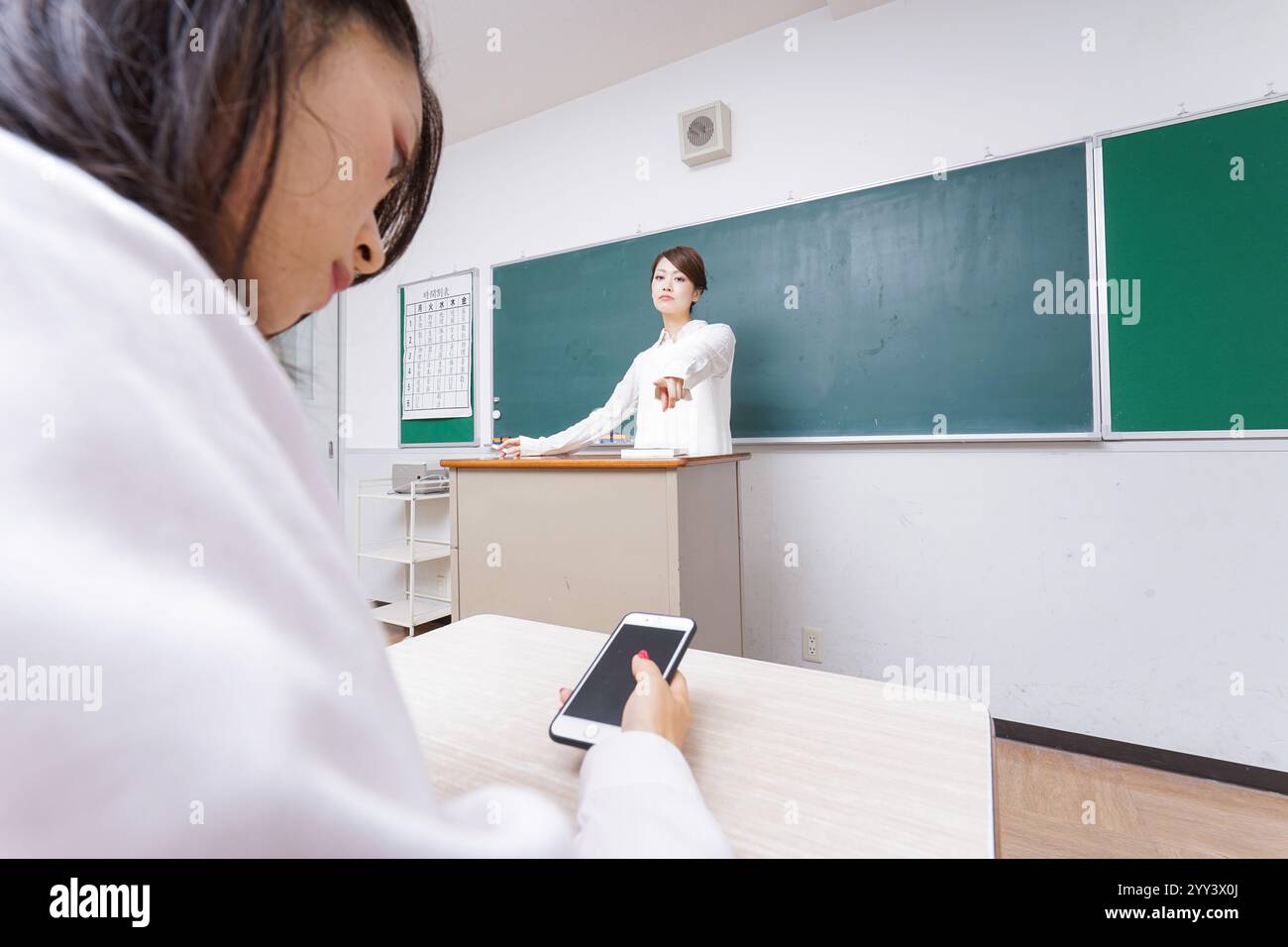 Student using a smartphone during class and teacher cautioning her ...