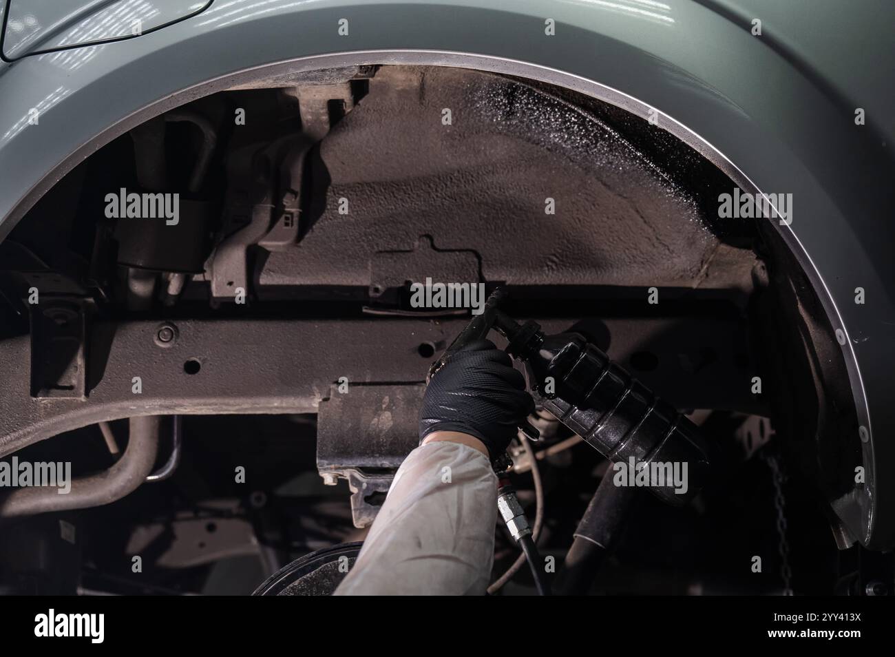 An auto mechanic applies anti-corrosion mastic to the underbody of a ...